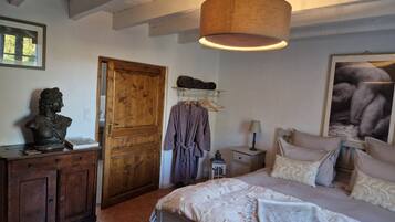 Quarto com cama, guarda-roupa de madeira, porta, mesa de cabeceira, abajur e um quadro na parede.