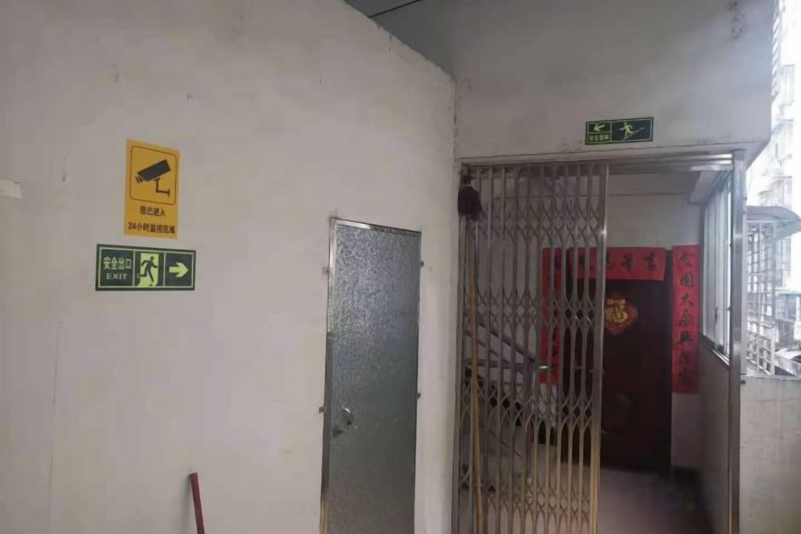 Corredor com placa de câmera de segurança, sinalização de saída e porta de metal.