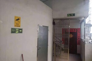 Corredor com placa de c âmera de segurança, sinalização de saída e porta de metal.