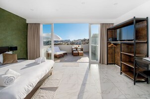 Quarto de hotel moderno com uma cama grande, uma varanda com vista, uma televisão e uma estante de livros.