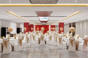Um amplo salão de banquetes com mesas e cadeiras redondas, paredes com detalhes em vermelho e centros de mesa florais.