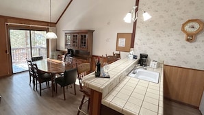 Uma sala de jantar com mesa e cadeiras de madeira, uma cozinha com bancada e pia azulejadas, e um armário de madeira.