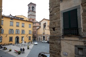 Uma rua estreita com edifícios amarelos, uma torre de sino e uma placa indicando 