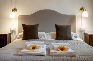 Cama bem arrumada com duas almofadas, duas toalhas dobradas com girassóis e abajures laterais.