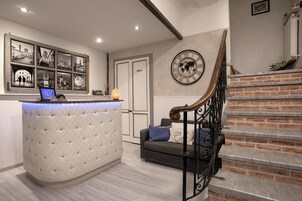 Uma área de recepção com uma mesa estofada, um relógio e uma escada.
