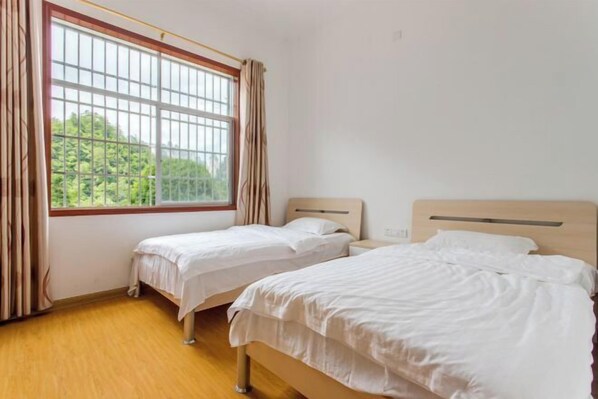 Quarto com duas camas de solteiro, uma janela grande com cortinas e piso de madeira.