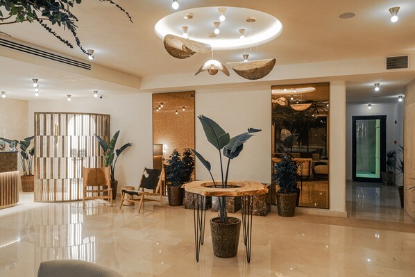 Um hall moderno com piso brilhante, balcão de recepção, áreas de estar e uma grande peça central com plantas.