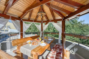 Um deck de madeira com uma mesa posta para o café da manhã, um banco e uma área coberta com ventilador de teto.