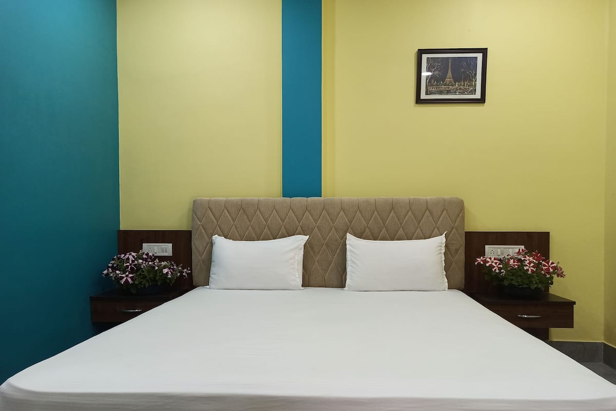 Cama com cabeceira acolchoada, duas almofadas e mesa de cabeceira com uma flor.