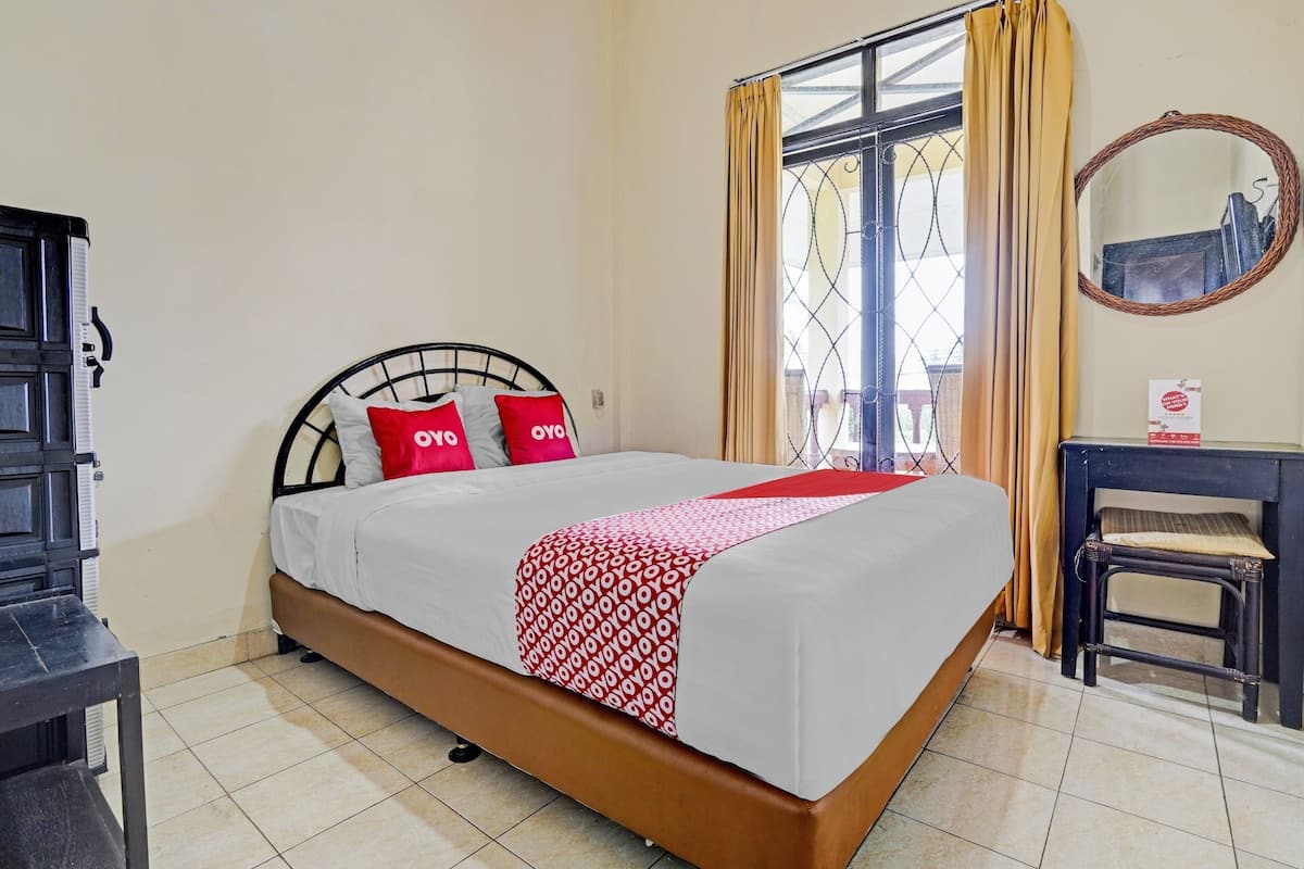 Quarto de hotel com cama, cadeira, mesa e janela com cortinas.