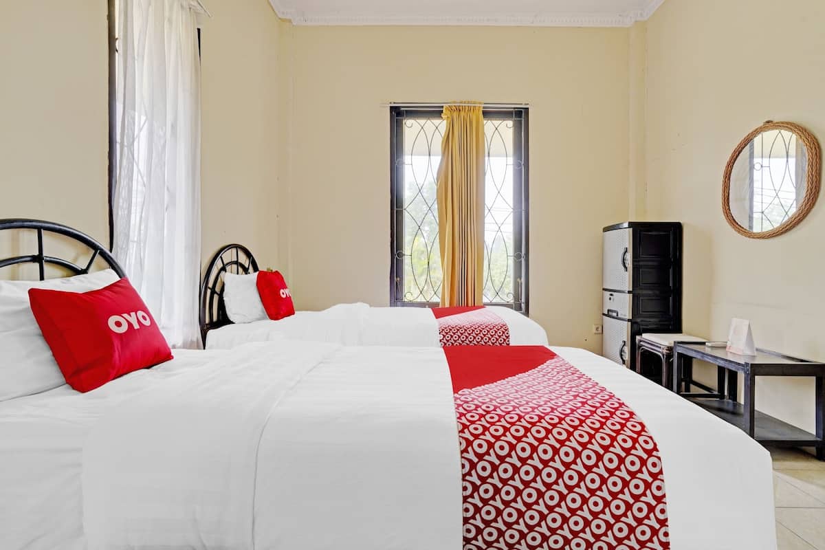 Quarto de hotel com cama, escrivaninha, guarda-roupa e janela com cortinas.