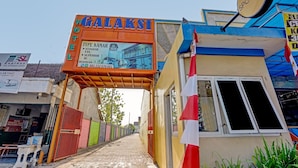 Edifício com uma placa indicando "GALAKSI" e "TYPE KAMAR", mostrando os tipos de quarto. Há uma bandeira e uma placa para "ESL Express" com um número de telefone.