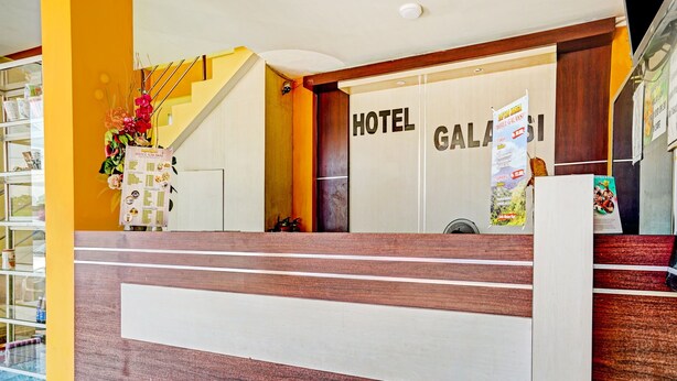 Balcão de recepção de hotel com bancada de madeira e uma placa com a inscrição 'HOTEL GALAXI'.
