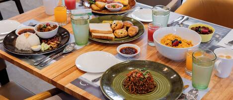 Mesa de jantar posta com diversos pratos, incluindo arroz, macarrão e pão, além de vários copos com bebidas.