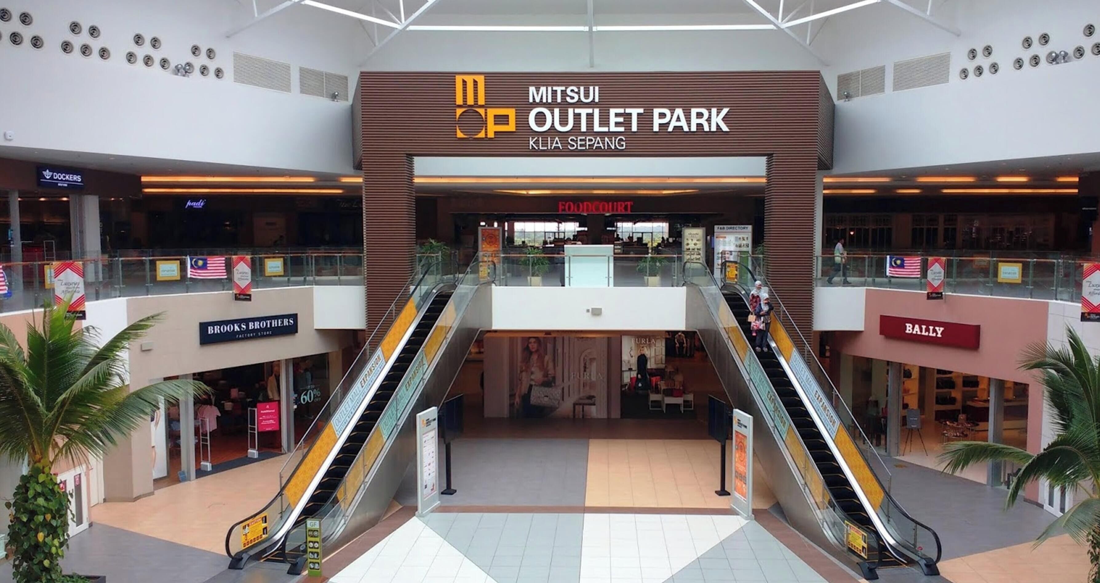 Interior de um shopping com a sinalização Mitsubishi Outlet Park, escadas rolantes e diversas lojas.
