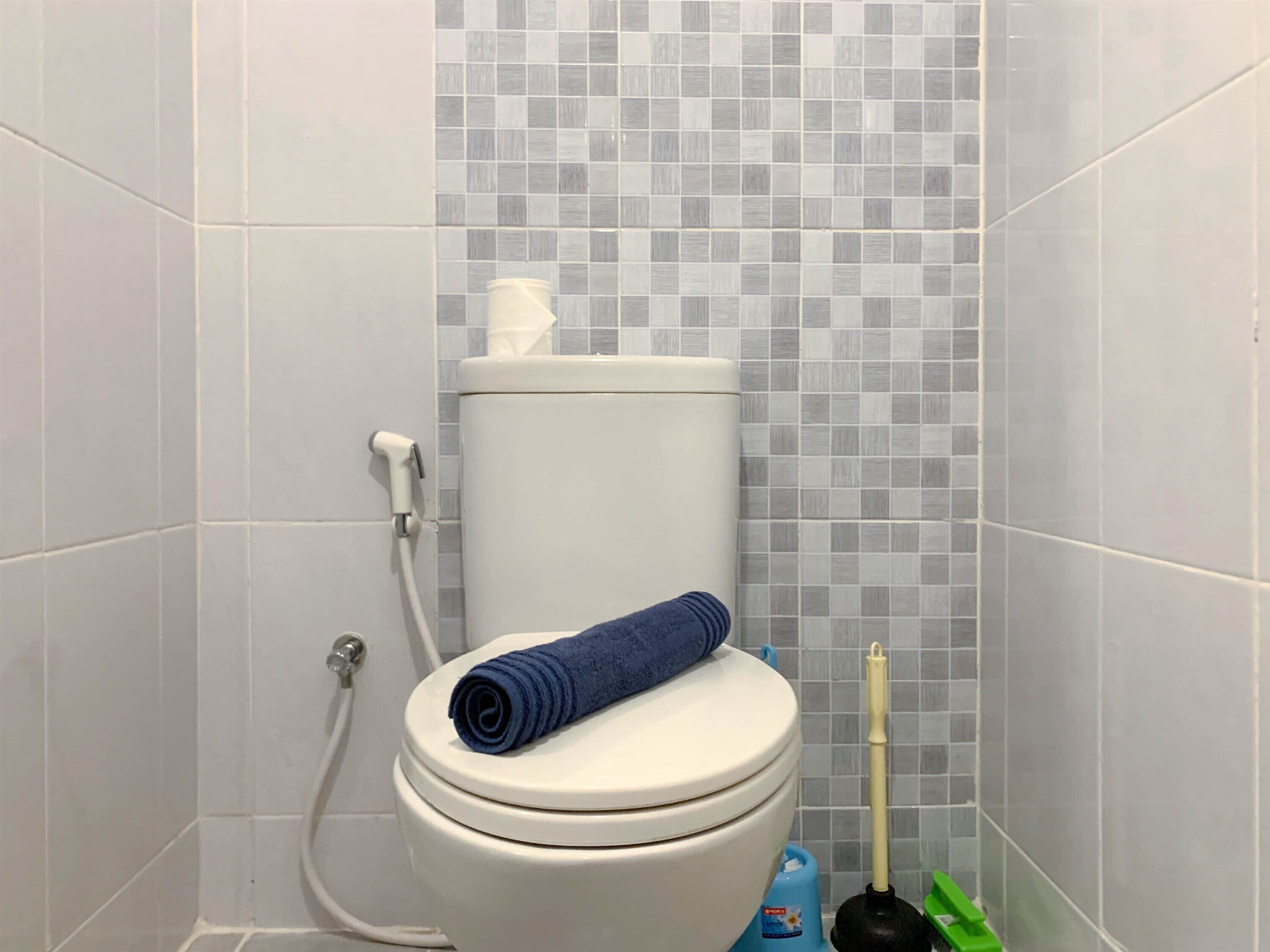 Casa de banho com sanita, uma toalha azul no assento, escova de sanita e desentupidor.