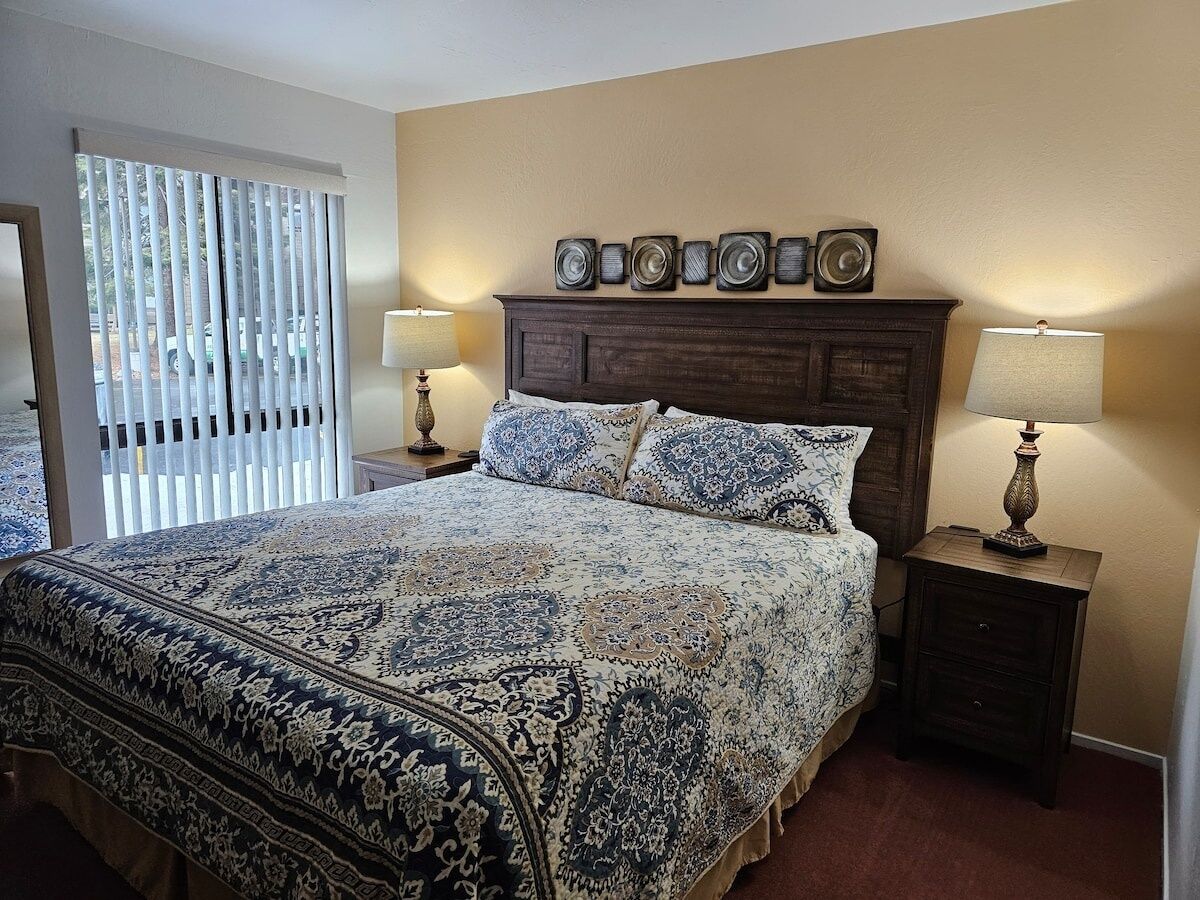 Quarto com cama grande, duas mesas de cabeceira com luminárias, cabeceira com pratos decorativos e janela com persianas.
