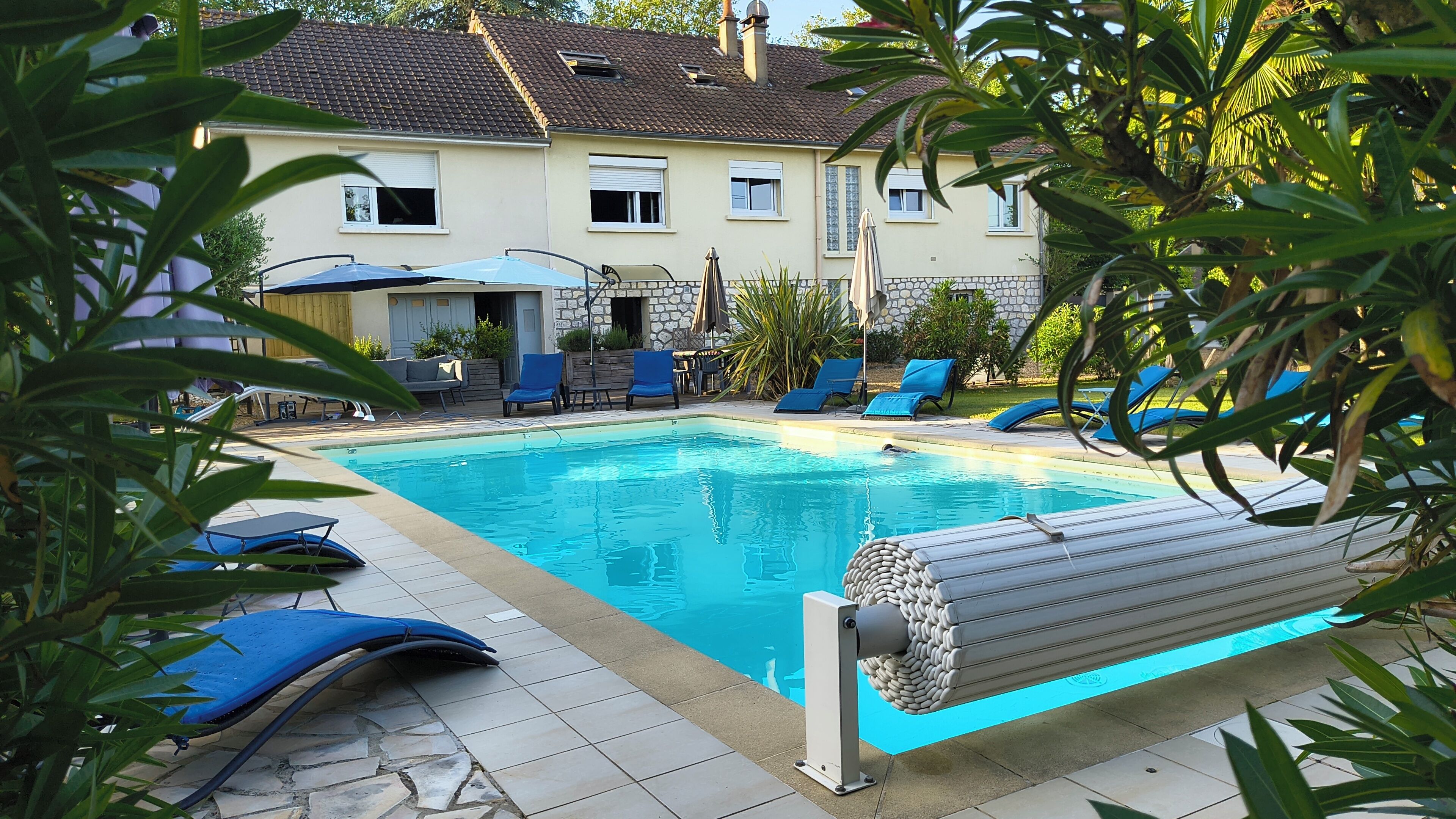 Piscina com espreguiçadeiras, um muro de pedra e um edifício ao fundo.