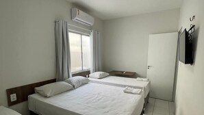 Quarto de hotel com duas camas, janela com cortinas, ar condicionado, televisão fixada na parede e chão em mosaico.
