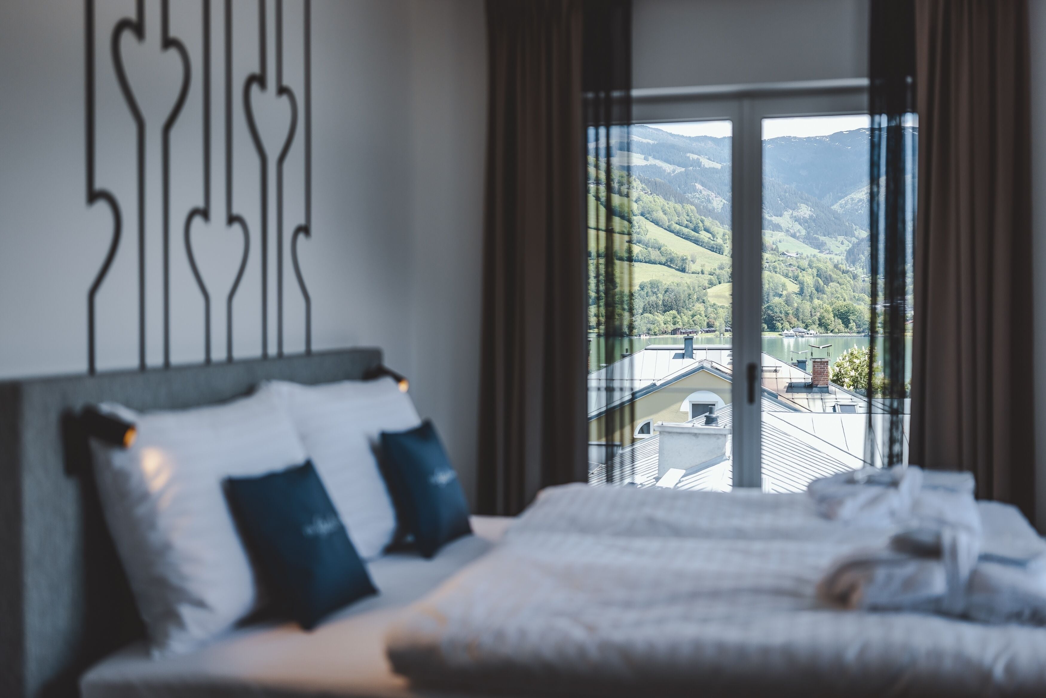 Quarto com cama, almofadas e vista para um lago e montanhas pela janela.