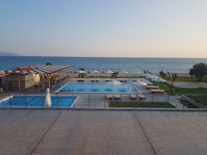Área da piscina com vista para o mar, mobiliário de jardim e um alpendre coberto.