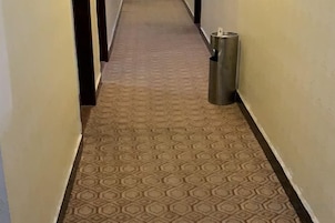 Um corredor estreito com carpete estampado e uma lixeira.