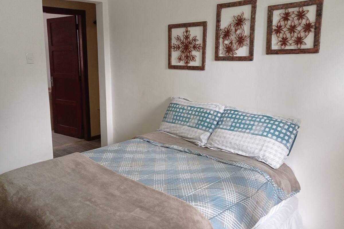 Quarto com cama, um banquinho de madeira e duas obras de arte de flores na parede.