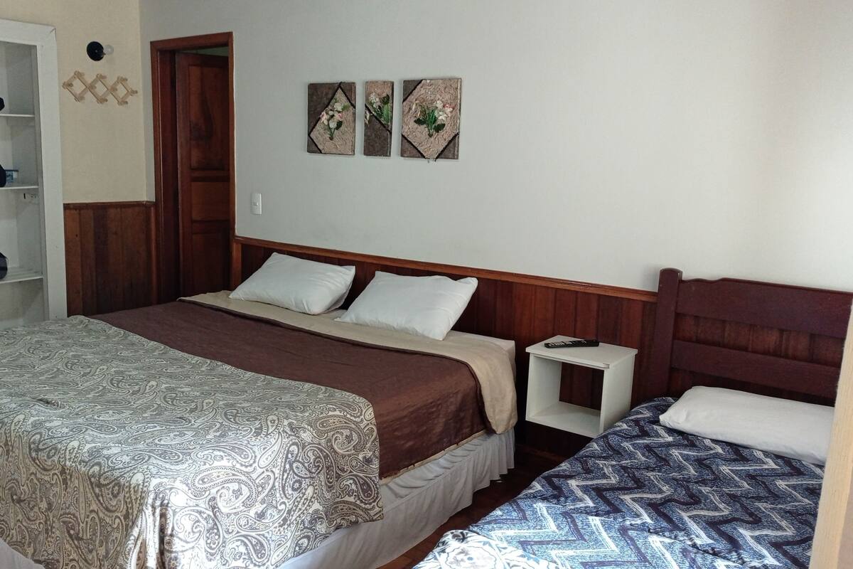 Quarto com uma cama grande, uma cama menor, um guarda-roupa e uma mesa de cabeceira.