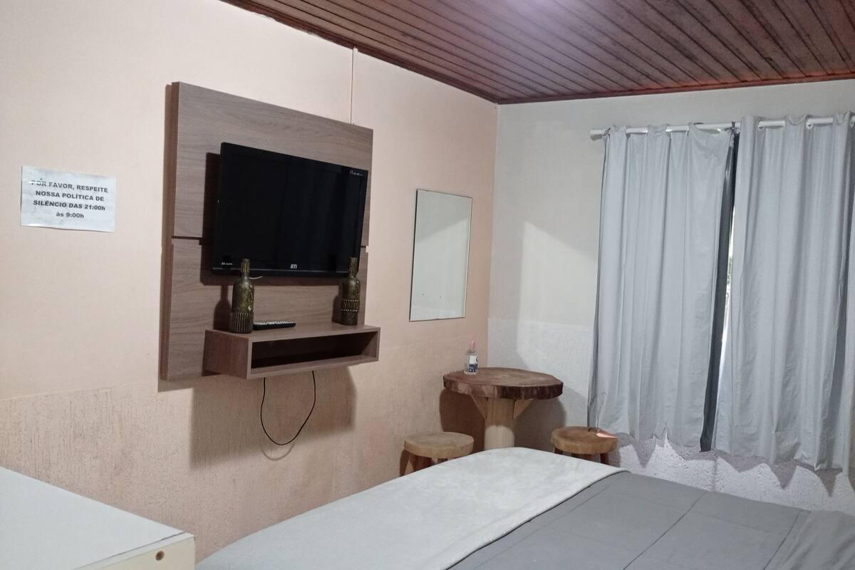 Quarto com cama, televisão na parede, mesa redonda pequena e espelho.