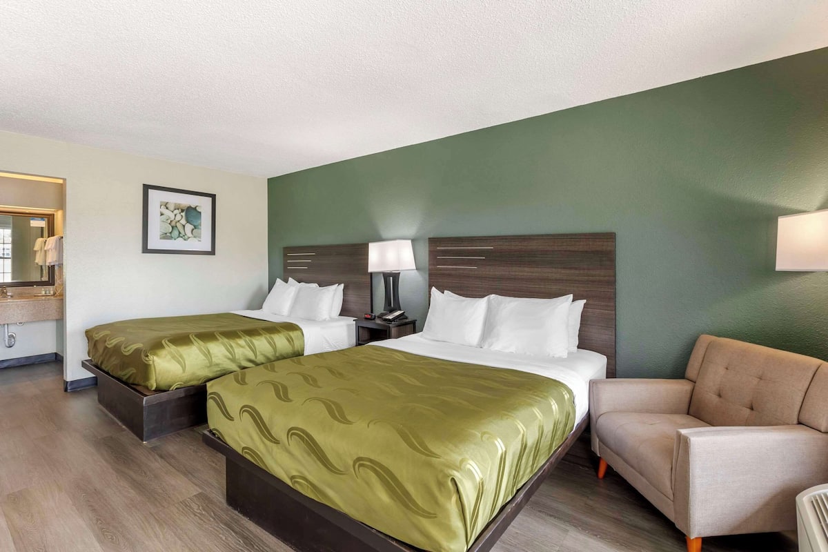 Quarto de hotel com duas camas de solteiro, um sofá, uma escrivaninha e um espelho.