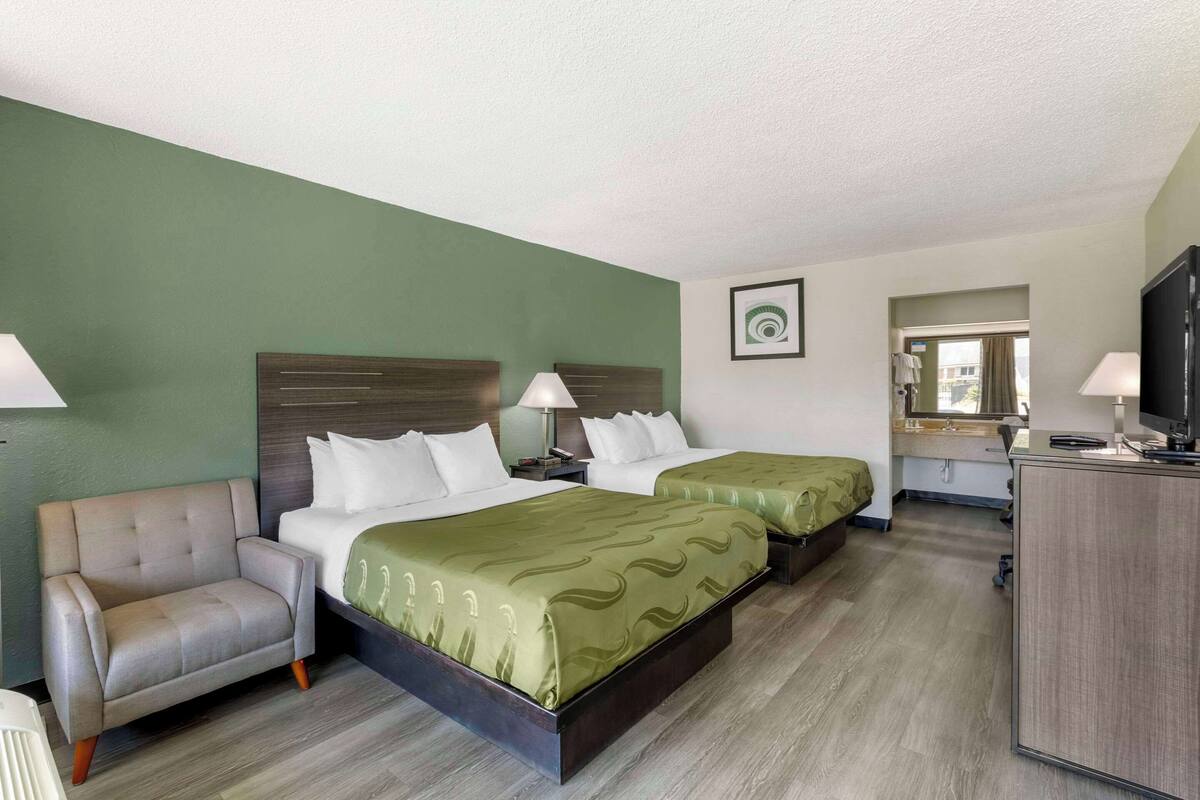 Quarto de hotel com duas camas, uma escrivaninha, uma cadeira e uma televisão.
