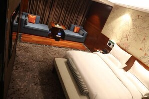 Quarto de hotel com cama, dois sofás, uma mesinha e parede com padrão floral.