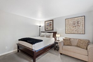 Um quarto com cama, mesa de cabeceira, luminária e sofá.