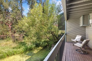 Varanda com vista para um jardim e árvores, deck de madeira e duas cadeiras.