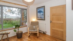 Quarto com uma janela grande, porta de madeira, radiador, cadeira e planta em vaso.