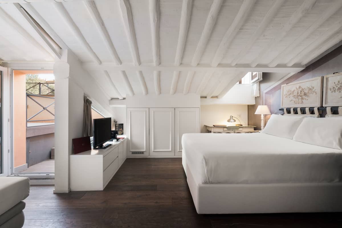 Quarto moderno com teto de madeira, cama, escrivaninha com televisão e janela.