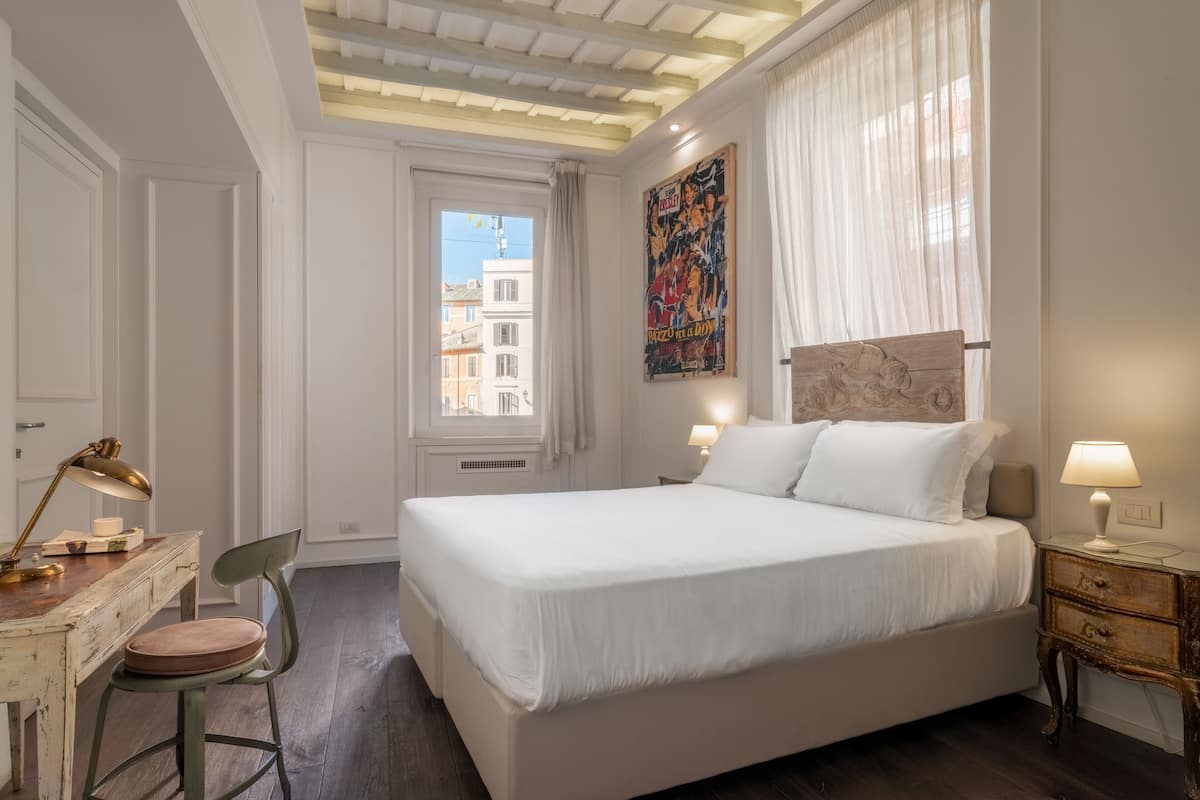 Quarto com uma cama grande, uma escrivaninha com cadeira, uma janela com cortinas e um quadro na parede.
