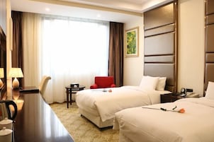 Quarto de hotel com duas camas, uma escrivaninha com abajur, uma mesinha e uma cadeira vermelha.