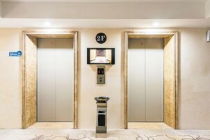 Um elevador com painel digital e botões, ladeado por duas portas e uma placa indicando o andar.