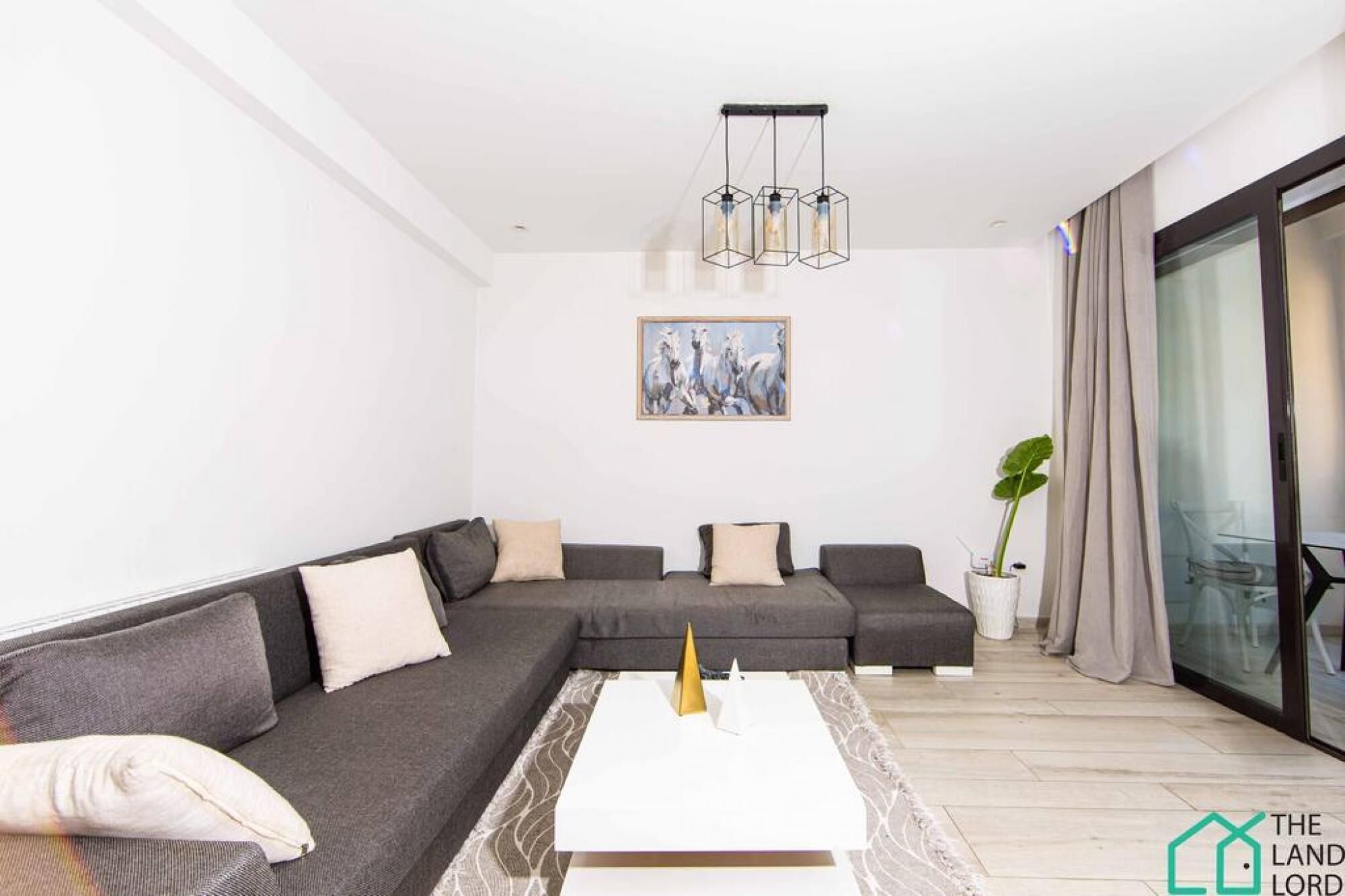 Uma sala de estar moderna com um sofá seccional, uma mesa de centro, um quadro e uma grande janela com cortinas.