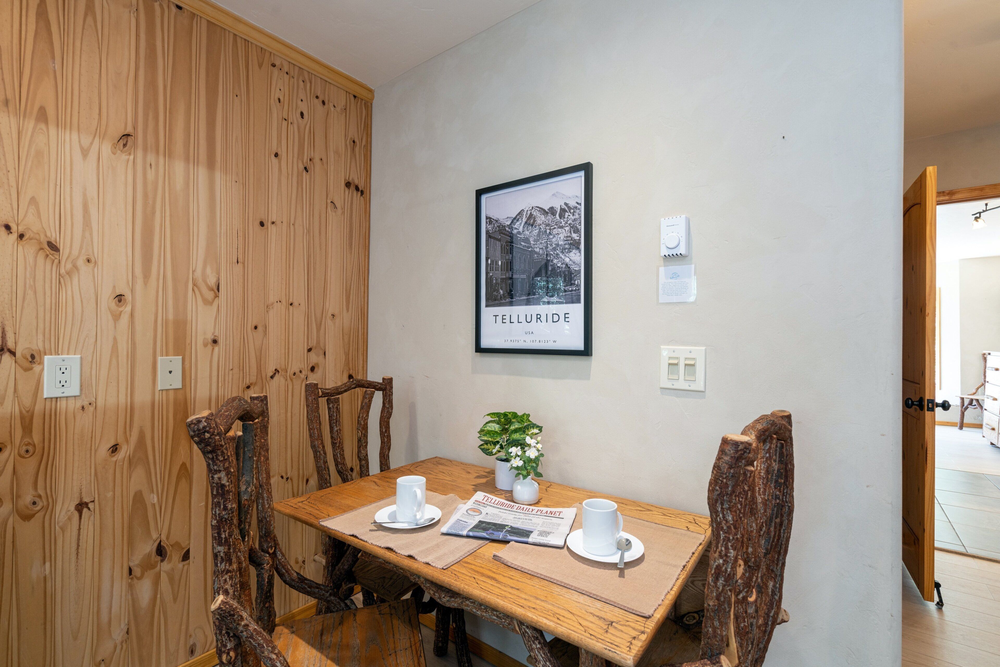 Uma mesa de jantar de madeira com cadeiras, um quadro emoldurado de Telluride, EUA, e uma pequena planta em vaso.
