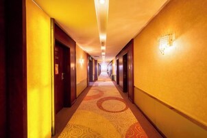 Corredor de hotel com portas em ambos os lados, iluminação no teto e carpete estampado.