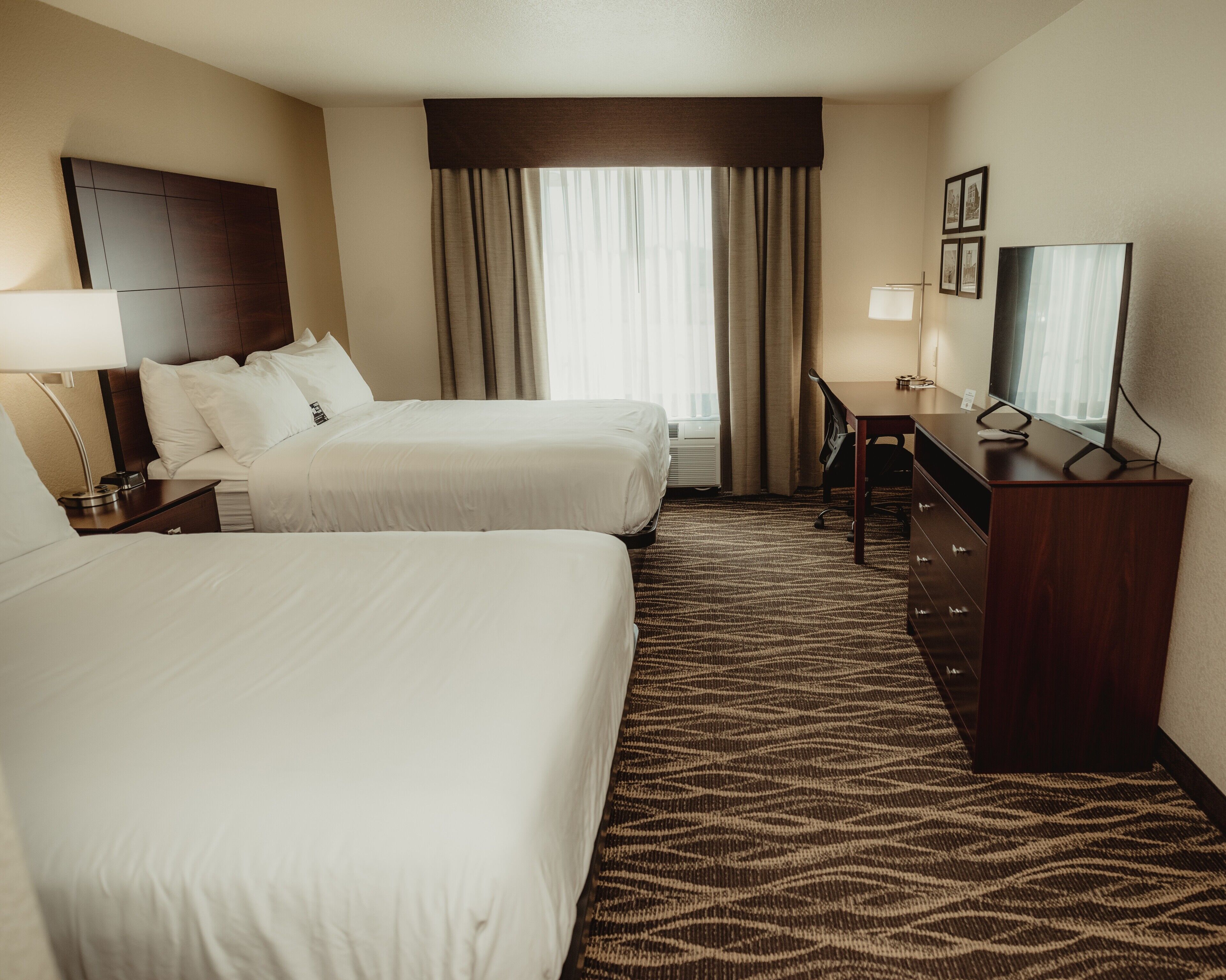 Quarto de hotel com duas camas, uma escrivaninha, cômoda e televisão.