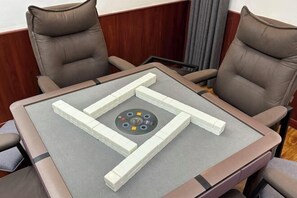 Um quarto com uma mesa quadrada, duas cadeiras de couro marrom e uma mesinha com um objeto branco em cima.