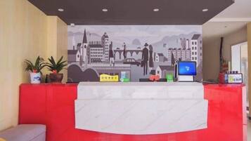 Balcão de recepção com um mural da paisagem urbana, um monitor de computador e um telefone.