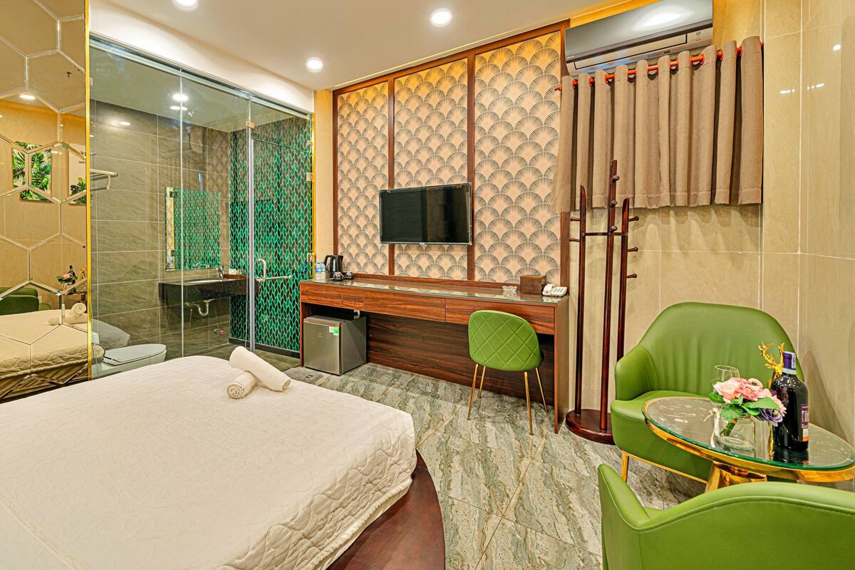 Quarto de hotel com cama, escrivaninha, cadeira, mesinha de centro com um vaso e televisão.
