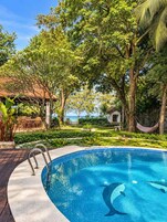 Piscina com design de golfinho, rodeada por vegetação exuberante e vista para o mar.