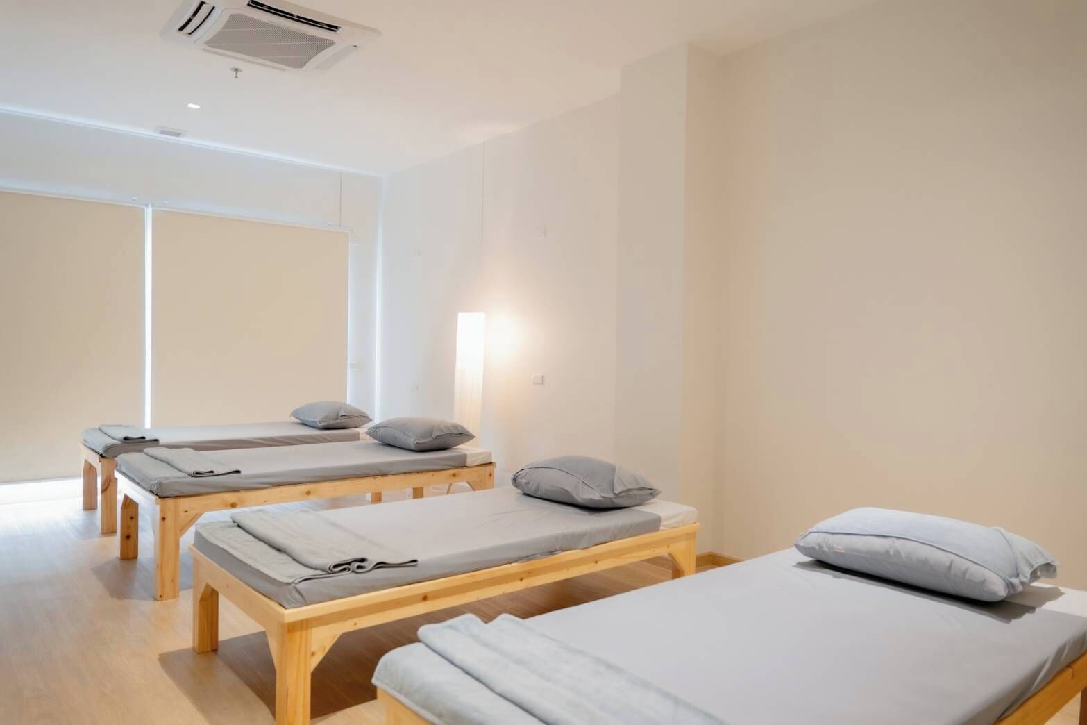 Um quarto com três camas de madeira, cada uma com colchão e travesseiro cinzas.