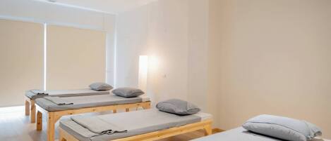 Um quarto com três camas de madeira, cada uma com colchão e travesseiro cinzas.