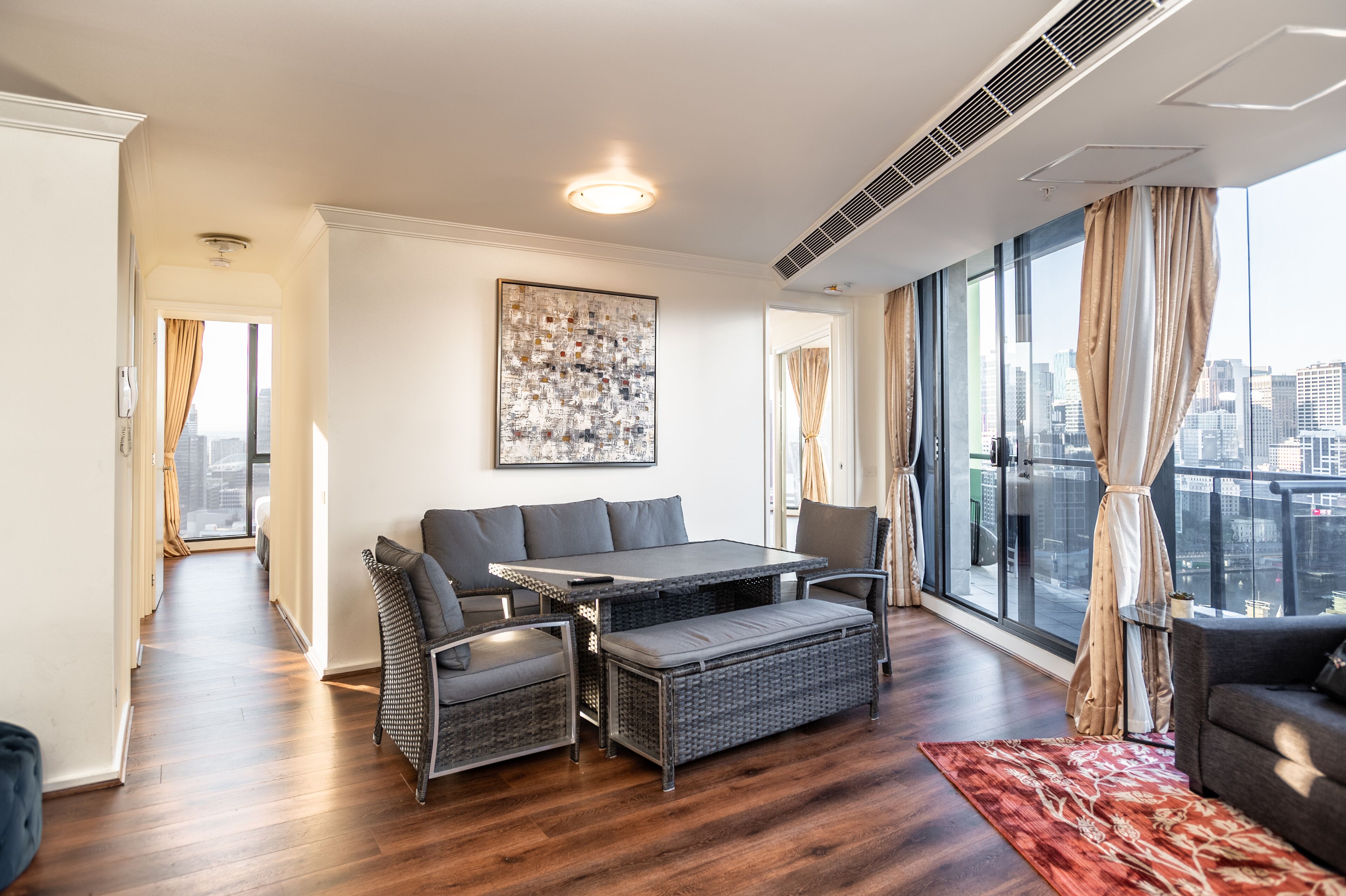 Uma sala de estar moderna com área de jantar, janelas amplas com cortinas e vista para a cidade.